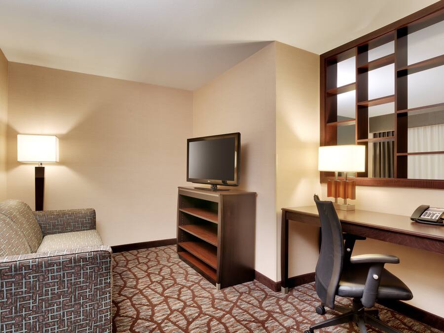 Quarto de hotel com uma cama, escrivaninha com telefone, televisão e uma cadeira.