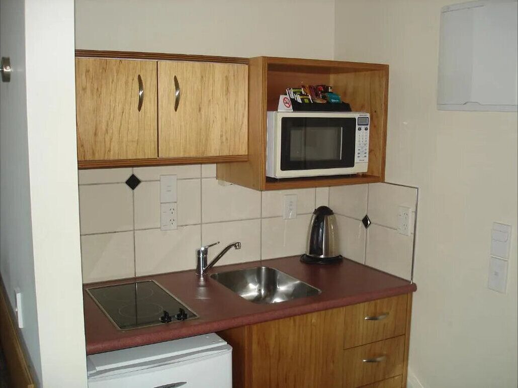 Cozinha compacta com armários de madeira, micro-ondas embutido, pia e chaleira.