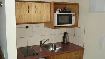 Cozinha compacta com armários de madeira, micro-ondas embutido, pia e chaleira.