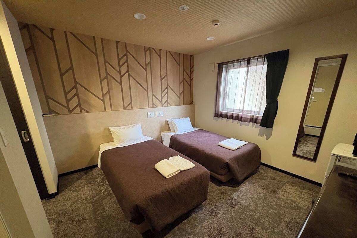 Quarto de hotel com duas camas, um espelho grande e uma janela com cortinas.