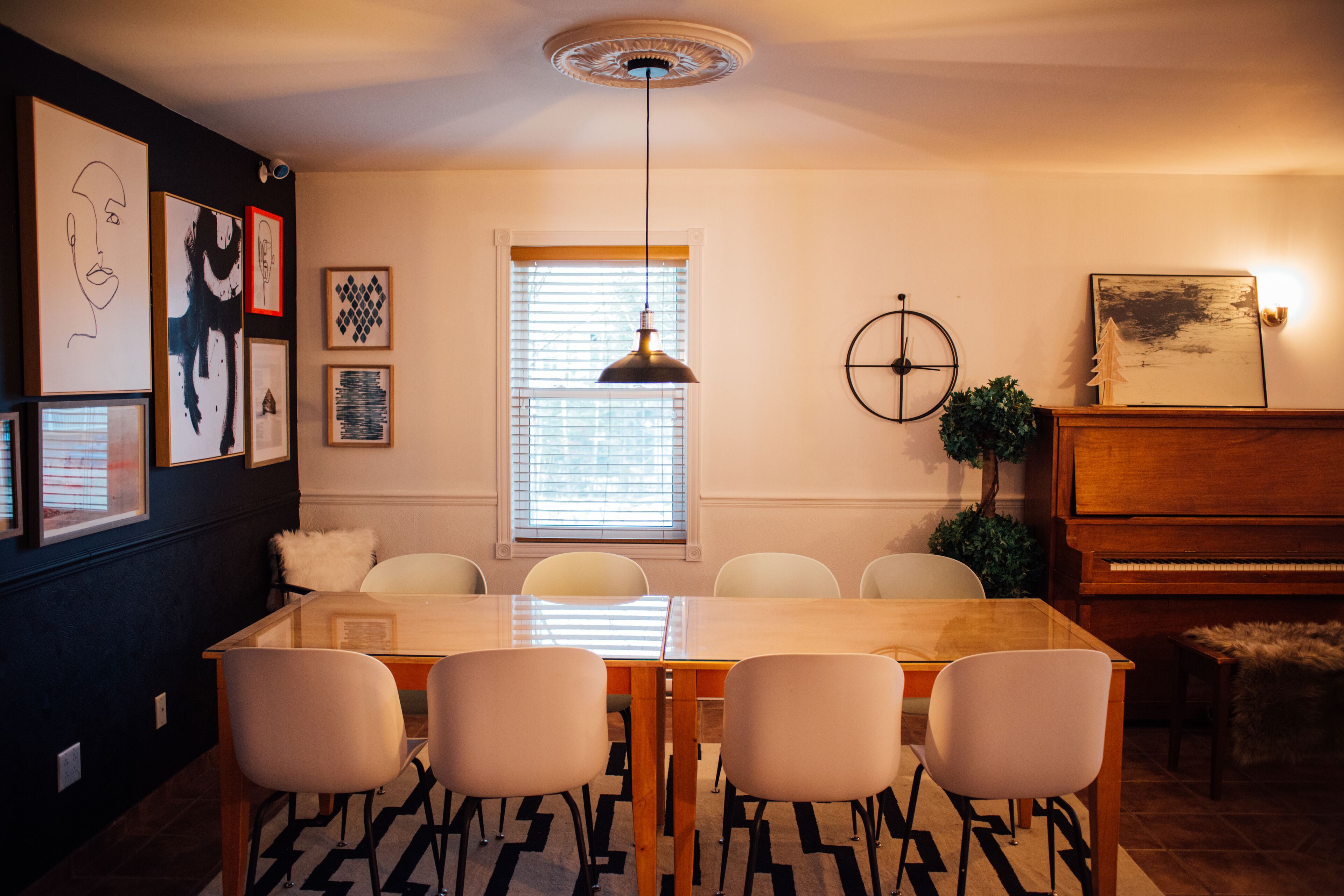 Uma sala de jantar com uma mesa retangular, seis cadeiras, uma luminária pendente e obras de arte emolduradas nas paredes.