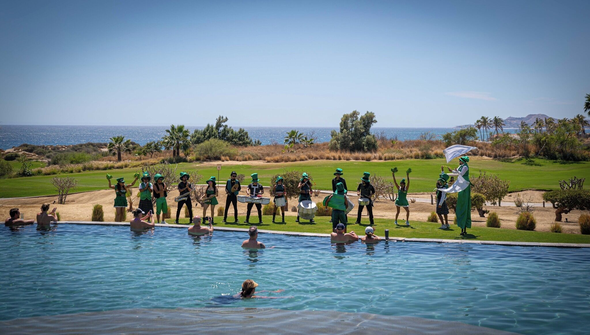 Piscina com pessoas de fato de treino, campo de golfe e vista para o oceano.