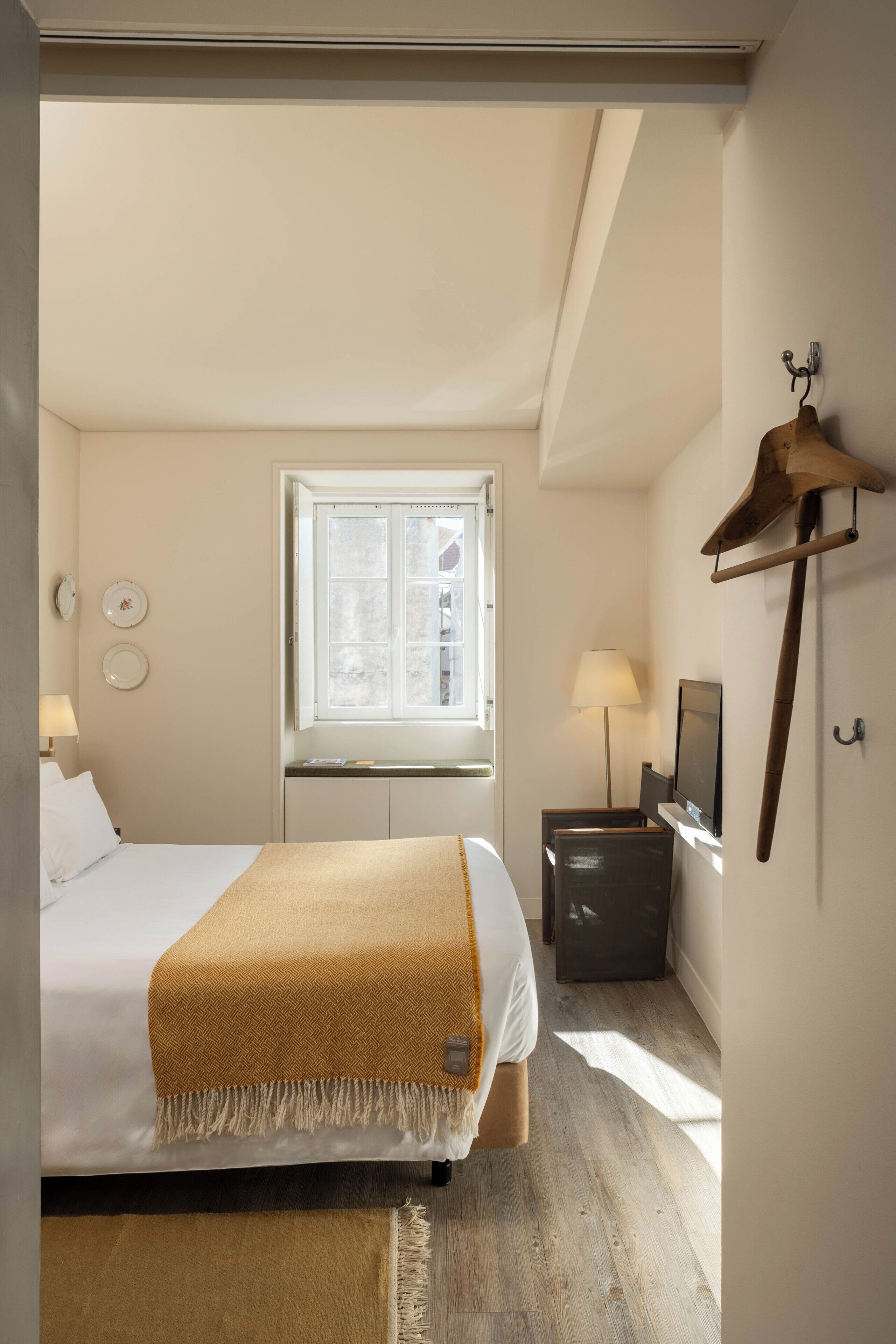 Quarto com cama, janela, mesa de cabeceira, luminária e cabideiro.