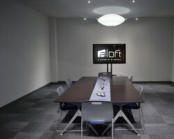 Uma sala de conferências com uma mesa comprida, cadeiras, uma tela de TV exibindo 'aloft' e um candelabro.