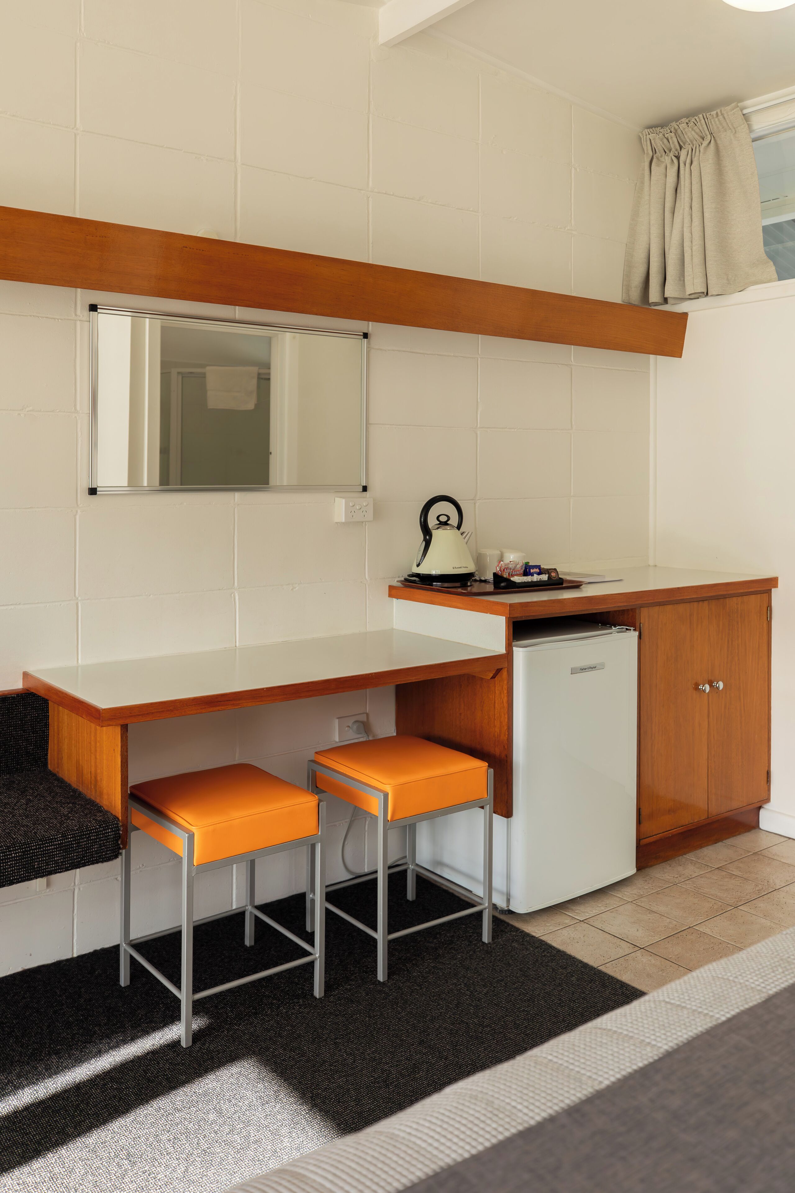 Uma cozinha compacta com geladeira branca, bancada de madeira e dois banquetes laranja.