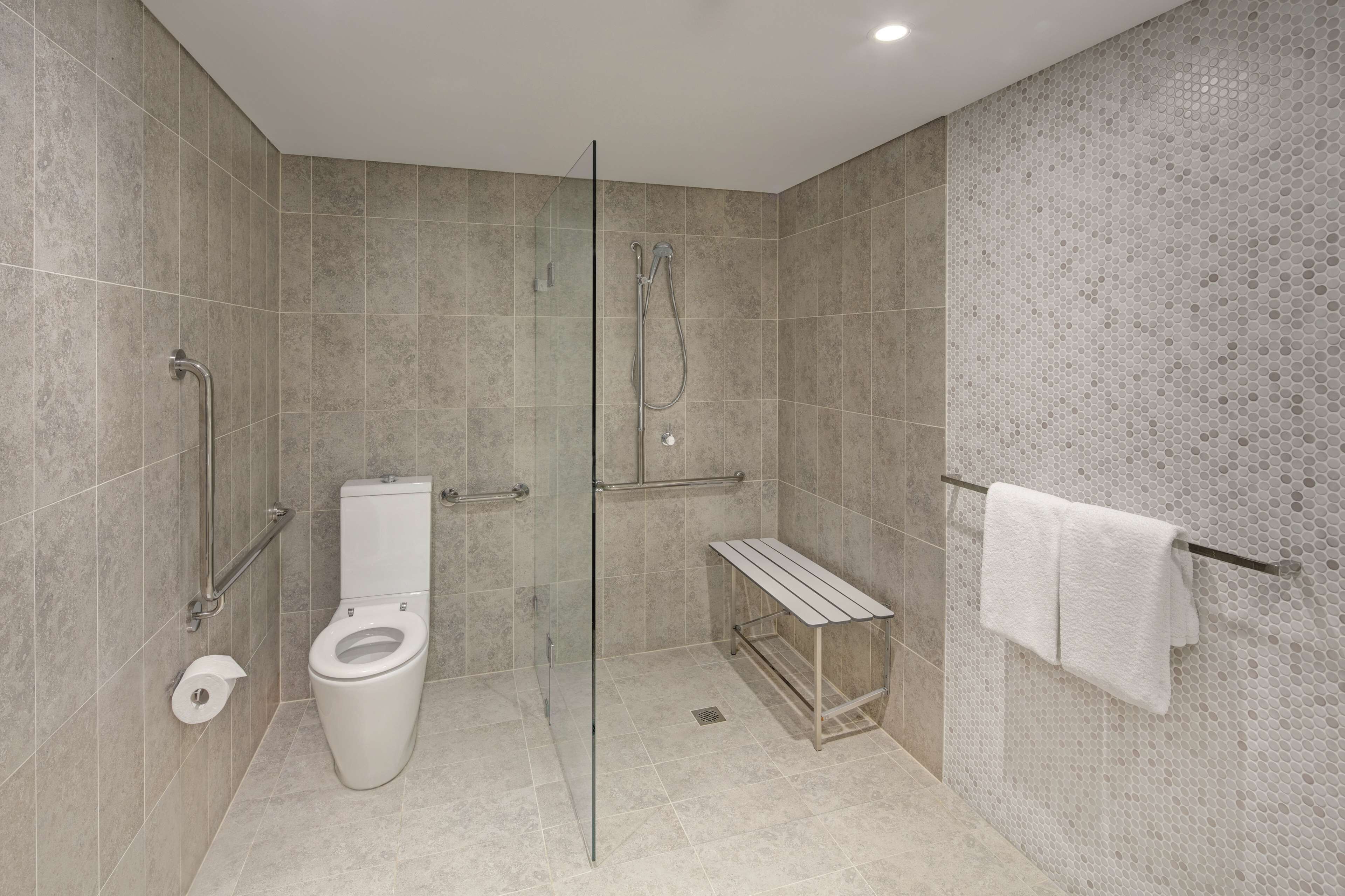 Casa de banho moderna com chuveiro individualizado por vidro, sanita e porta-toalhas.