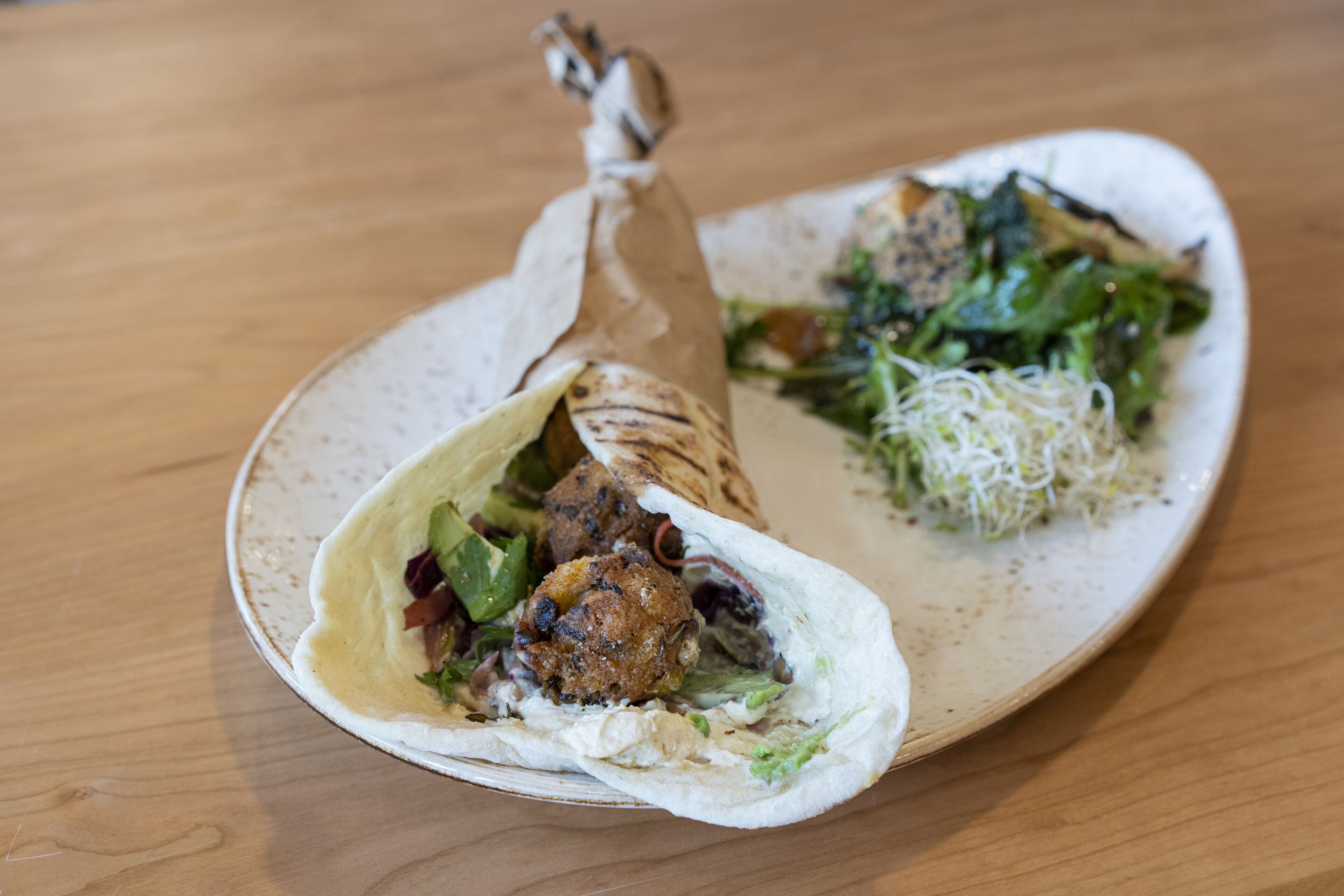 Um prato com um wrap recheado de carne e legumes, acompanhado de uma salada com folhas verdes e brotos.
