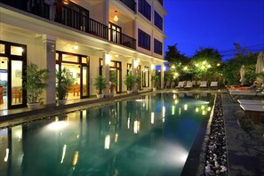 Vista noturna de um hotel com piscina, área de estar ao ar livre e varandas bem iluminadas.