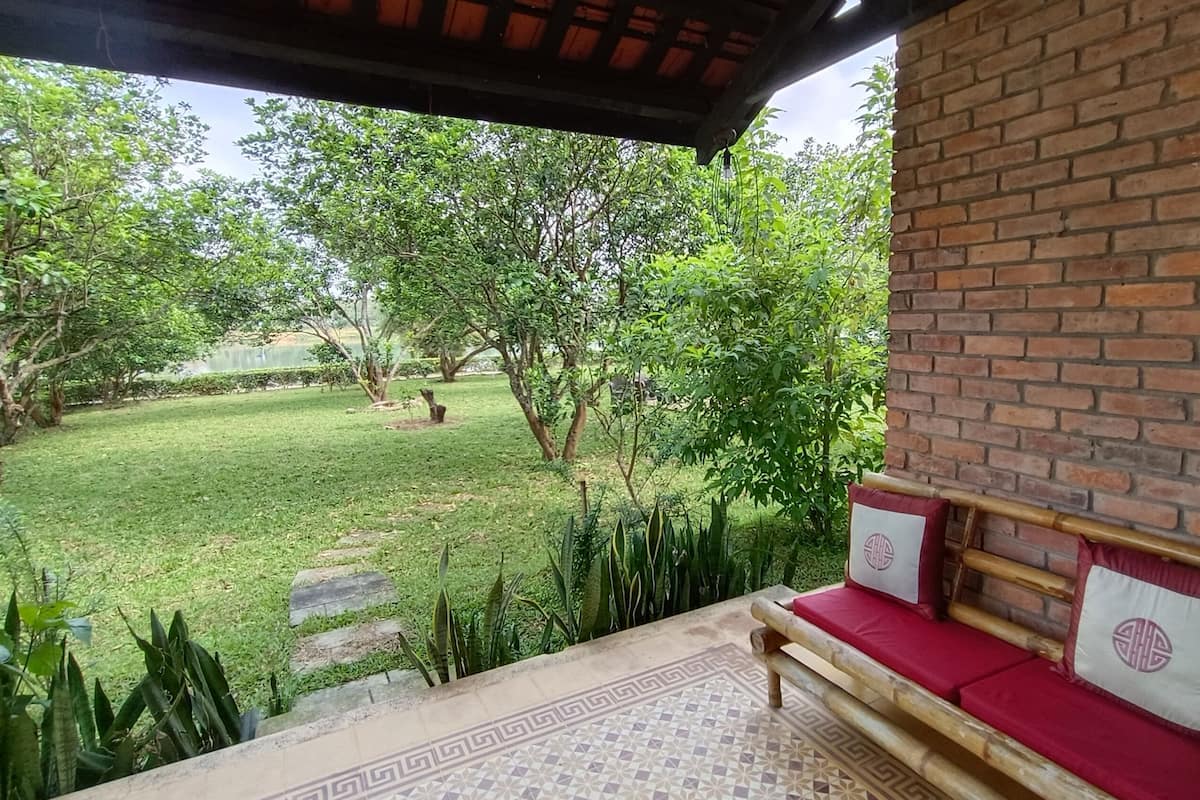 Área de estar coberta ao ar livre, com parede de tijolos e vista para um jardim exuberante.