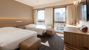 Quarto de hotel com duas camas, uma escrivaninha, uma cadeira, uma janela grande com vista para a cidade e uma televisão de tela plana.