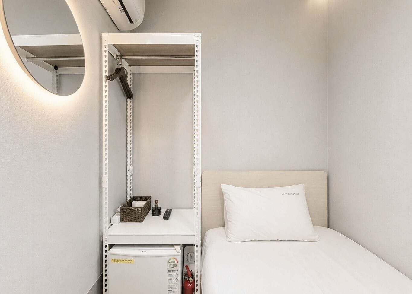 Quarto pequeno e compacto com uma cama de solteiro, mesa de cabeceira e estante.