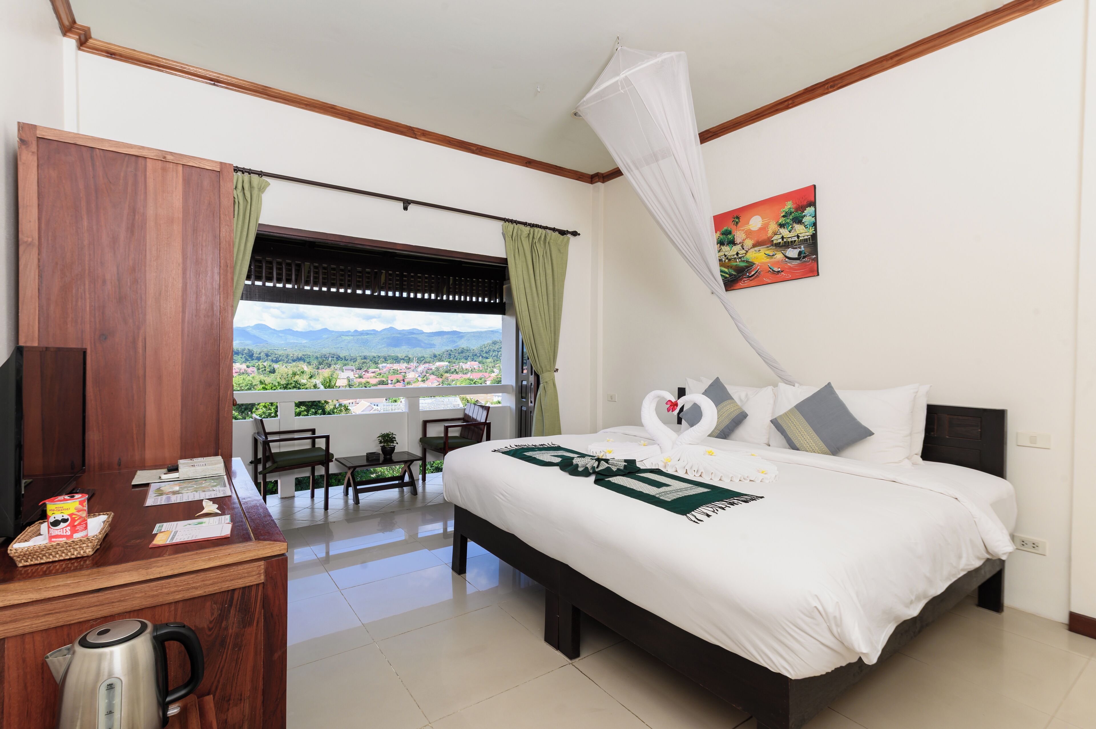 Quarto de hotel com cama, escrivaninha com chaleira, cadeira e vista para as montanhas, além de mosquiteiro.