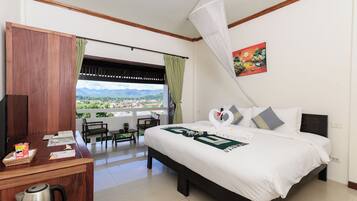 Quarto de hotel com cama, escrivaninha com chaleira, cadeira e vista para as montanhas, além de mosquiteiro.