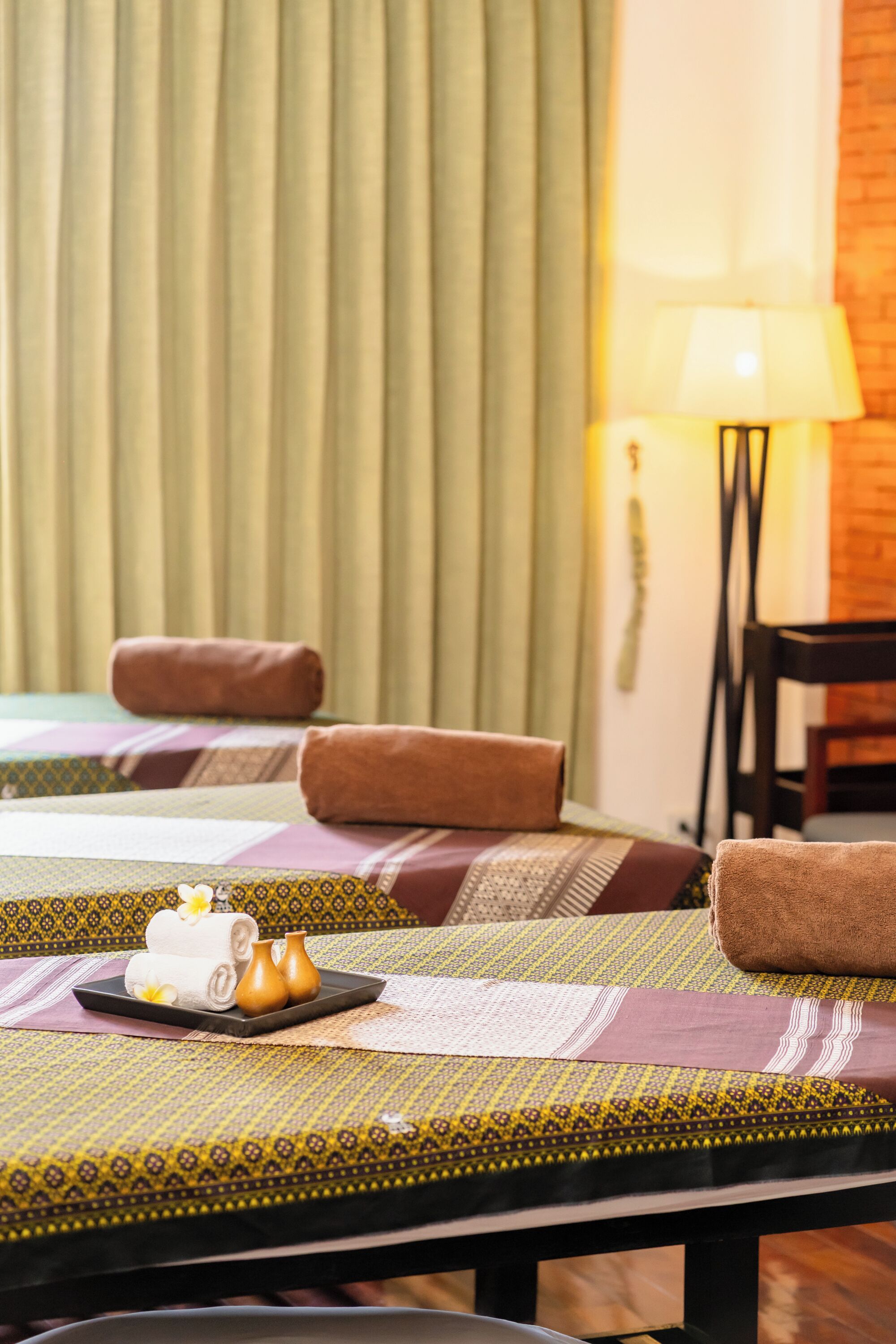 Quarto de hotel com duas camas, cada uma com colcha estampada e toalha enrolada. Uma bandeja com toalha e dois vasos está colocada sobre a cama.