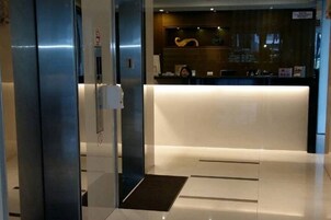 Uma área de recepção com design moderno, com balcão de atendimento, tela digital e divisória de vidro.