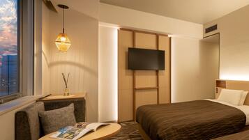 Quarto de hotel com uma cama, televisão, escrivaninha com abajur e janela com vista para a cidade.
