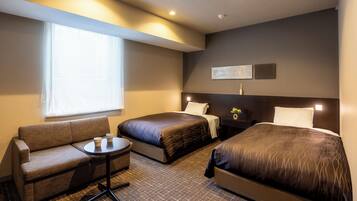 Quarto de hotel com duas camas, um sofá, uma mesa pequena e uma janela com cortinas.