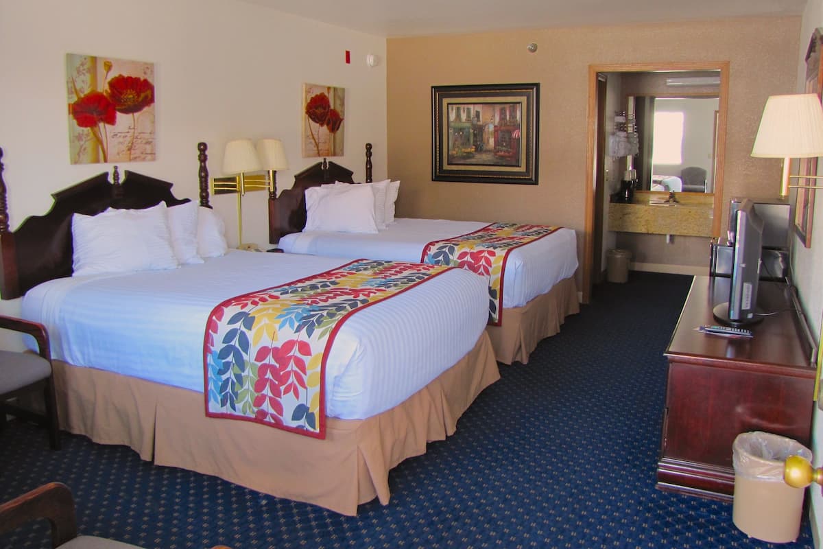 Quarto de hotel com duas camas, uma escrivaninha, uma cadeira, uma luminária, um cesto de lixo e um quadro na parede.