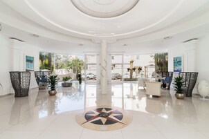Um hall amplo com um pilar central, áreas de estar e plantas em vasos.