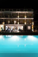 Hotel com vários andares, piscina em primeiro plano. Possui várias varandas e fachada bem iluminada.
