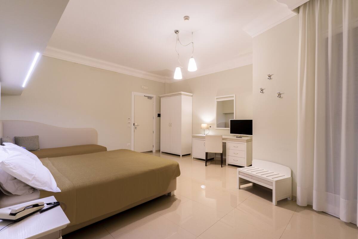 Quarto de hotel com duas camas, uma mesa, uma cadeira, uma televisão e a porta do banheiro.