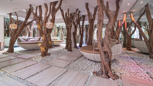 Um jardim interno moderno com estruturas de árvores de madeira, assentos de vime e um caminho de pedras.