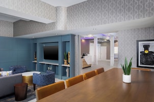 Uma sala de estar moderna com uma grande mesa de jantar de madeira, móveis azul e cinza e uma TV de tela plana na parede.