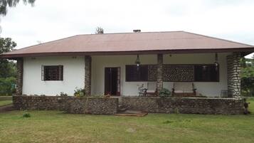 Uma casa térrea com base de pedra, telhado vermelho e varanda com dois bancos.
