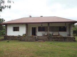 Uma casa térrea com base de pedra, telhado vermelho e varanda com dois bancos.