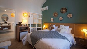 Quarto com cama, mesas de cabeceira, escrivaninha, espelho e enfeites de parede.