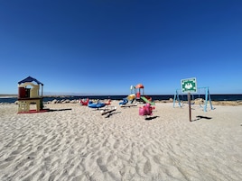 Uma praia com uma torre salva-vidas, escorregadores infláveis e baloiços.