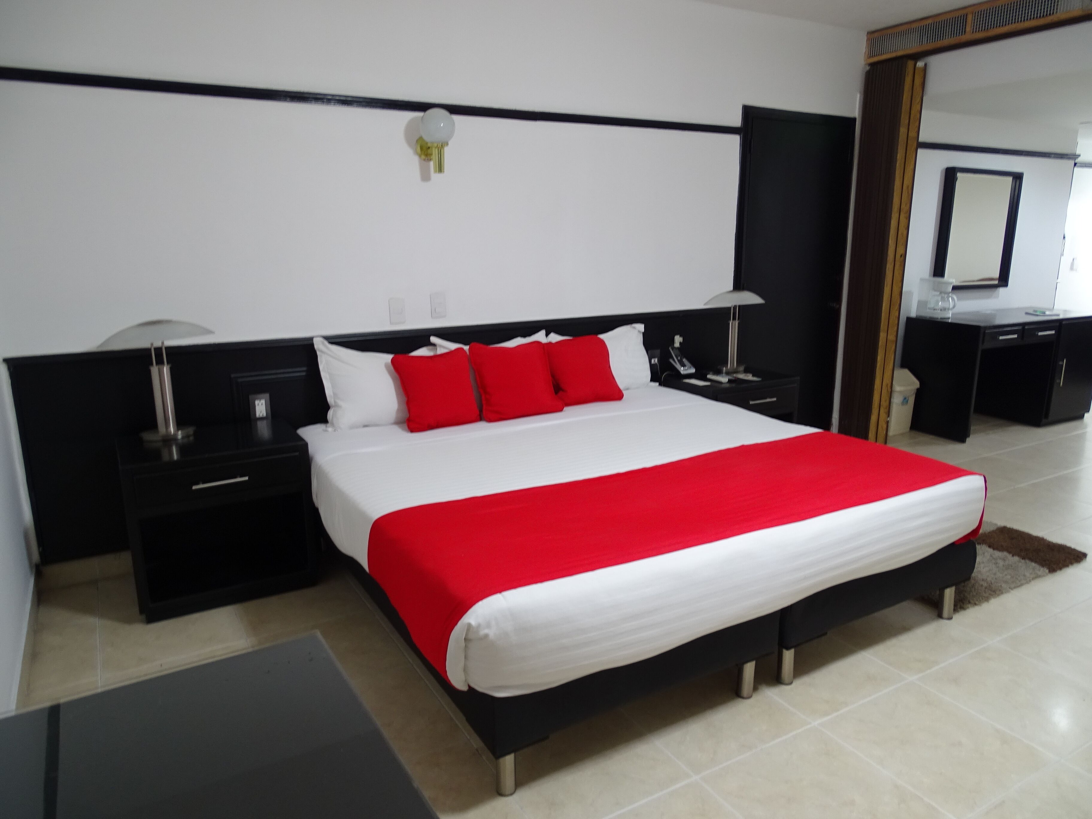 Quarto de hotel moderno com uma cama grande, mesas de cabeceira pretas, uma escrivaninha e um espelho.