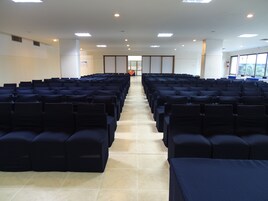 Uma sala de conferências com fileiras de cadeiras pretas e piso de azulejos.