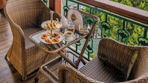 Varanda com móveis de vime, uma mesa posta com doces, um bule e uma xícara.