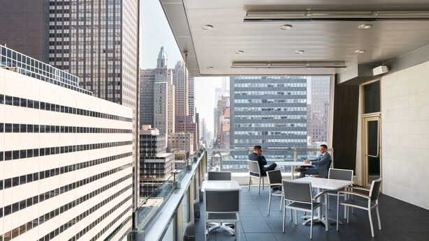 Terraço moderno no telhado com vista para a cidade, com mesa e cadeiras para refeições ou reuniões.