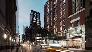 Hotel moderno com fachada de vidro, exterior de tijolos e entrada visível com uma placa.