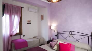Quarto com duas camas de solteiro, janela com cortinas cor-de-rosa, ar-condicionado fixado na parede, luminária de cabeceira e um objeto decorativo na parede.