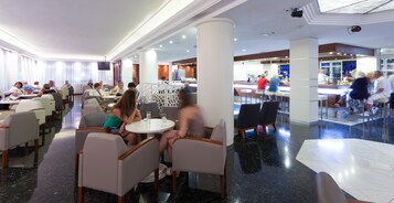 Um amplo hall de hotel com várias áreas de estar, um bar central e vista para o bar.