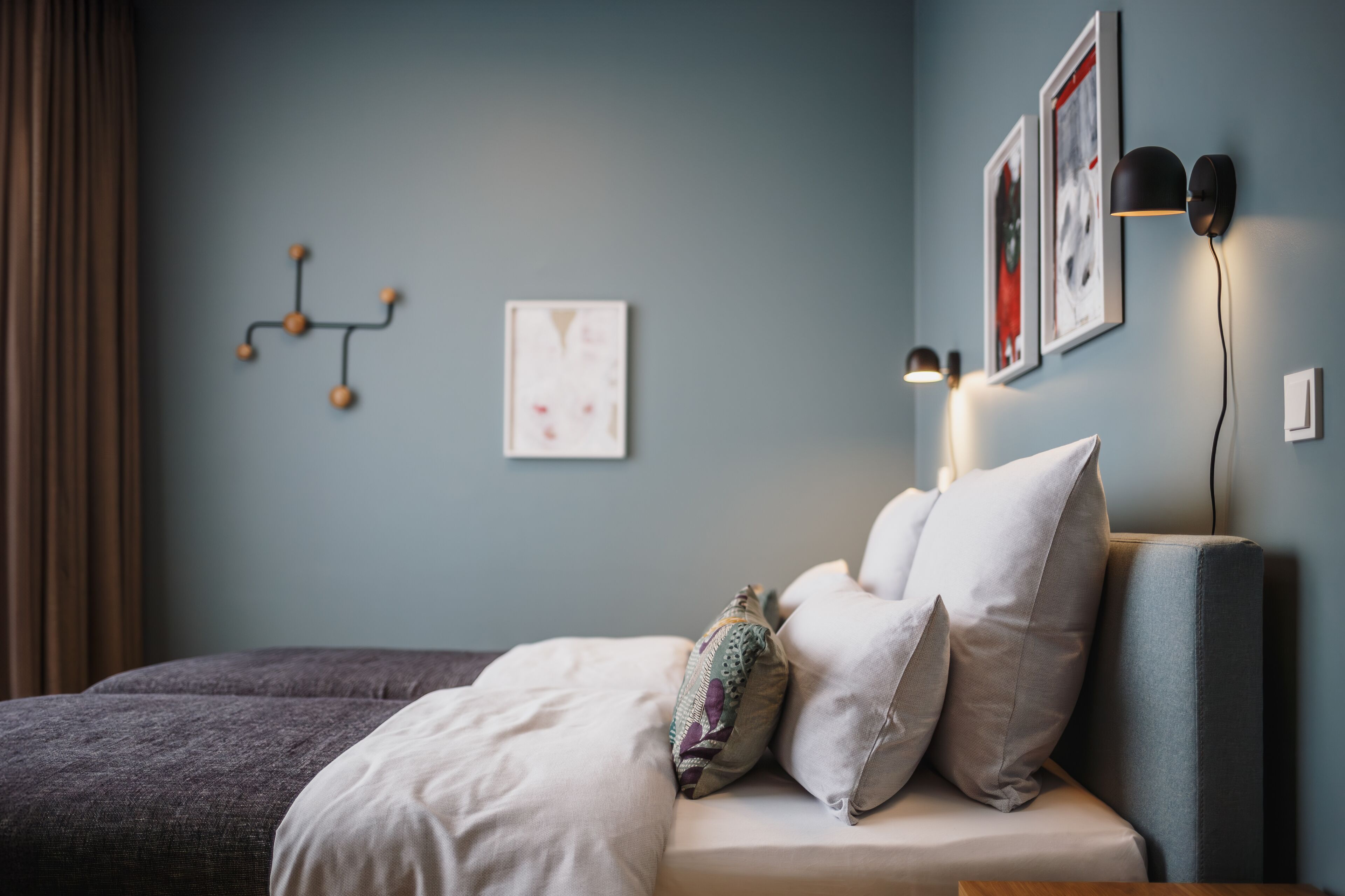 Quarto com cama, almofadas, luminária na parede e duas fotos emolduradas.