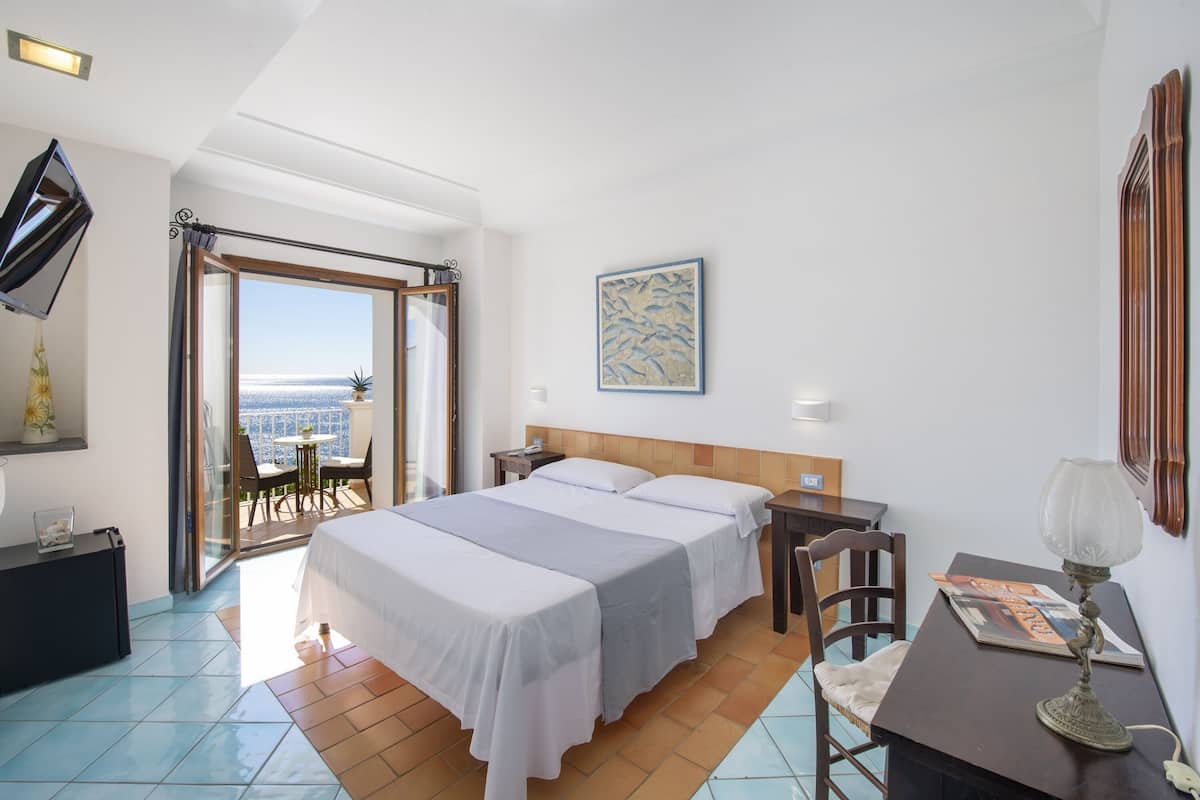 Quarto de hotel com cama, escrivaninha, cadeira, mesa, televisão e janela com vista.