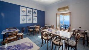 Uma sala de jantar com paredes azuis, várias mesas e cadeiras. Há impressões botânicas emolduradas nas paredes.