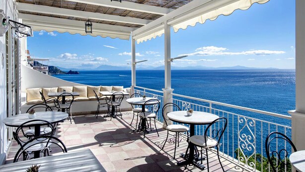 Terraço com área externa, mesas e cadeiras com vista para o mar.