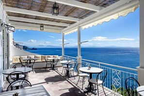 Terraço com área externa, mesas e cadeiras com vista para o mar.