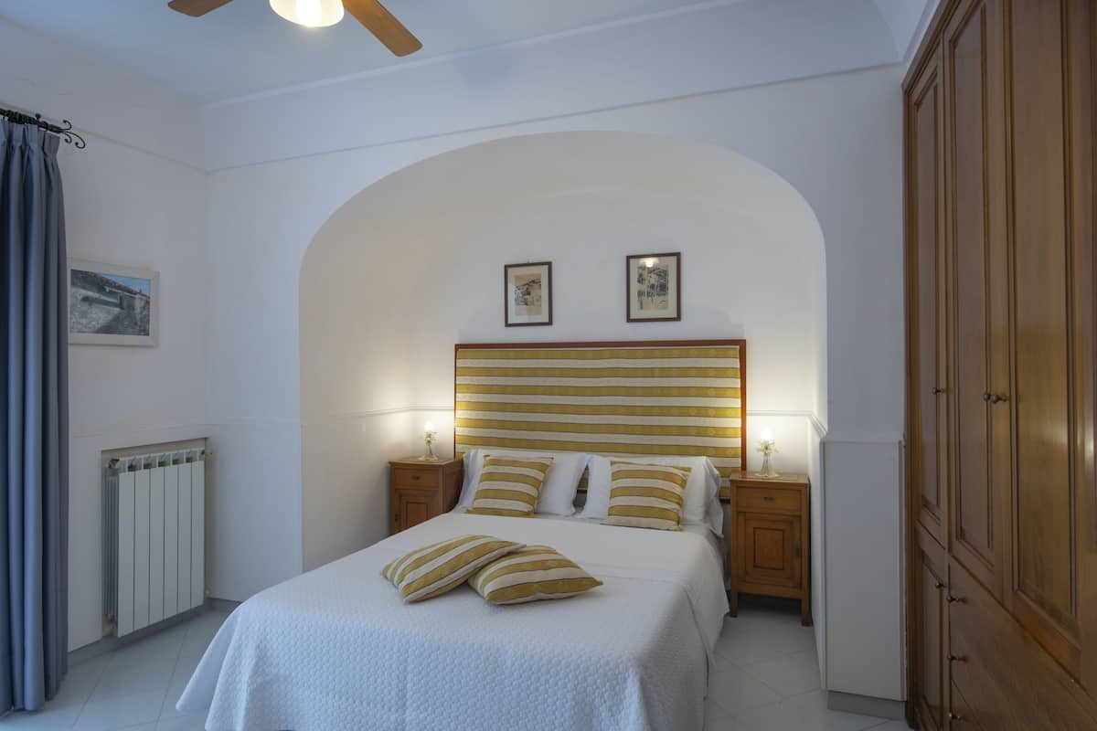 Quarto com uma cama, duas mesas de cabeceira, um radiador e um guarda-roupa.