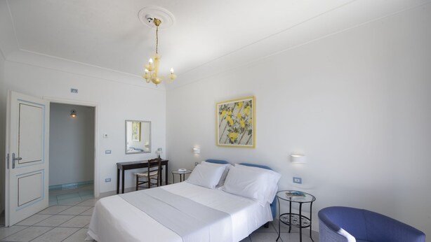 Quarto de hotel com uma cama grande, uma escrivaninha, uma cadeira, uma mesa pequena e um candelabro.