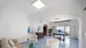 Uma sala de estar ampla com uma janela grande, um sofá, uma mesa de centro e uma mesa de jantar com cadeiras.