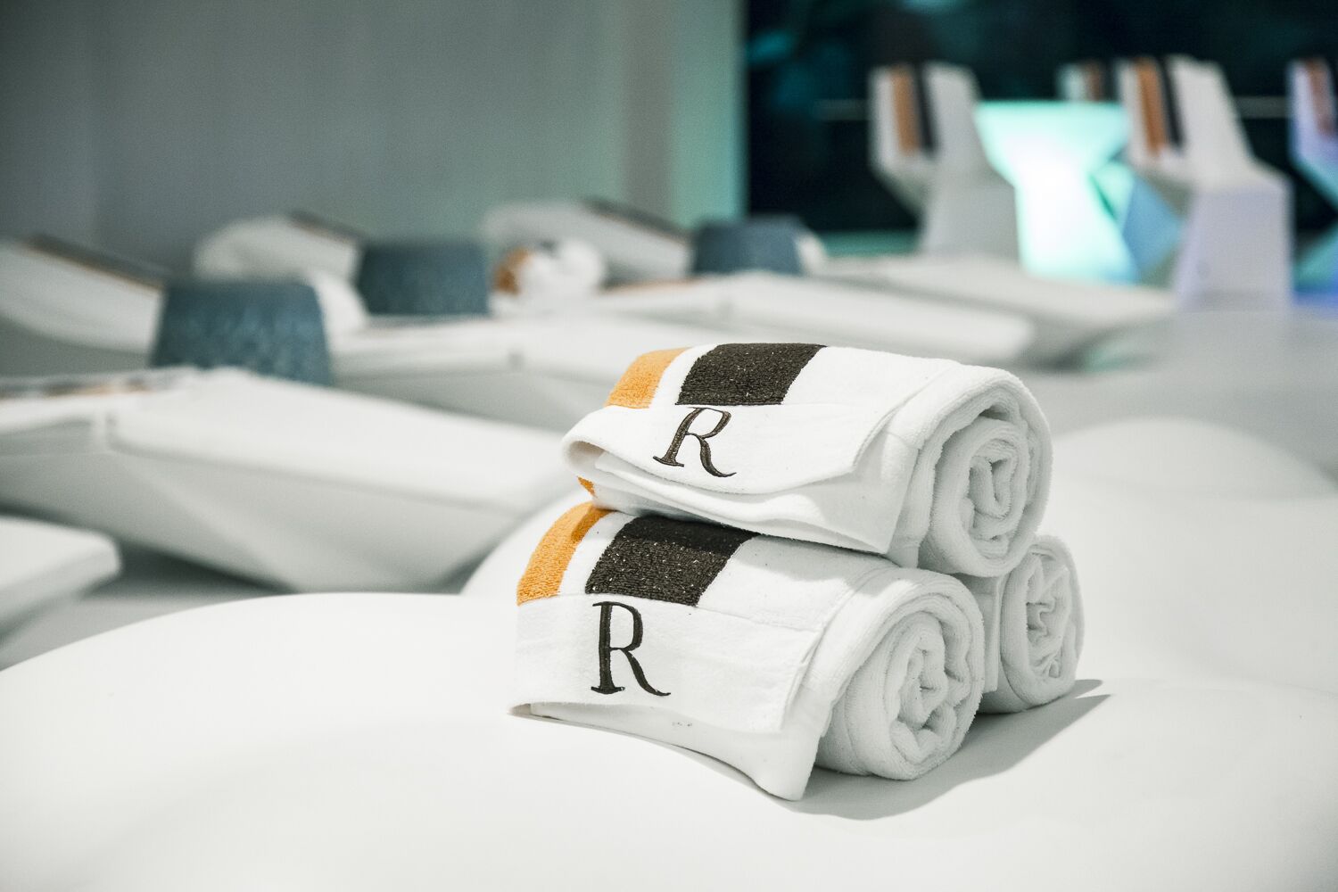 Toalhas dobradas com a letra 'R' em superfície branca de quarto de hotel.