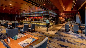 Um restaurante moderno com área de bar, várias mesas de jantar e um tapete estampado.