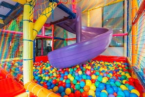 Uma área de recreação interna colorida, com um escorrega roxo e uma piscina de bolinhas cheia de bolas de várias cores.