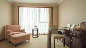 Quarto de hotel com sofá, mesa de vidro, escrivaninha e cadeira.